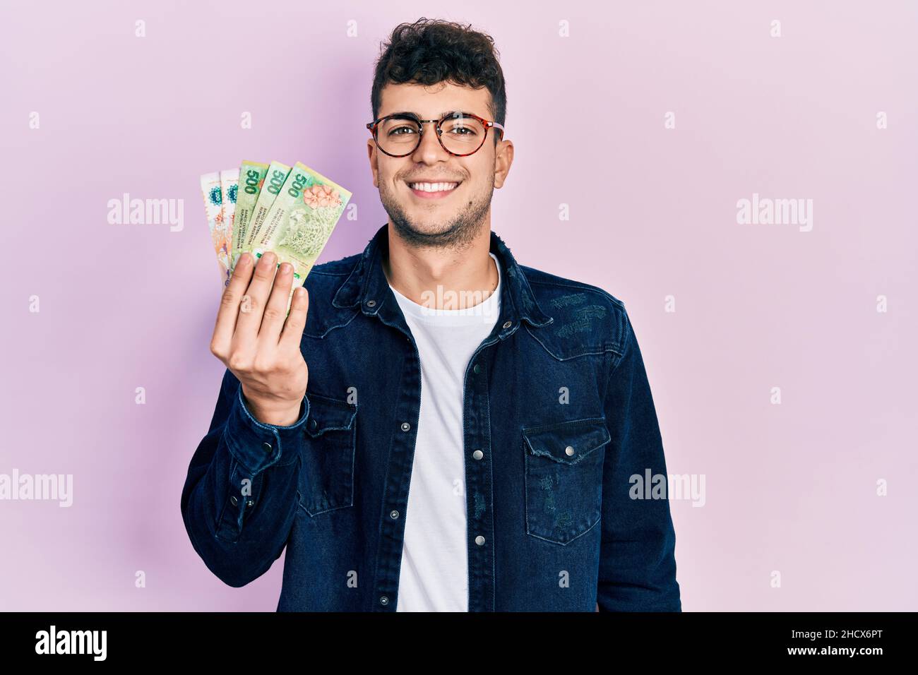 Young hispanic man holding argentine pesos banknotes looking positive ...
