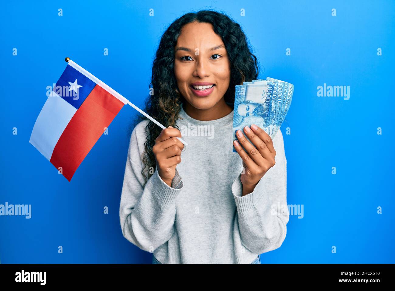 Young latin woman holding chile flag and chilean pesos banknotes ...