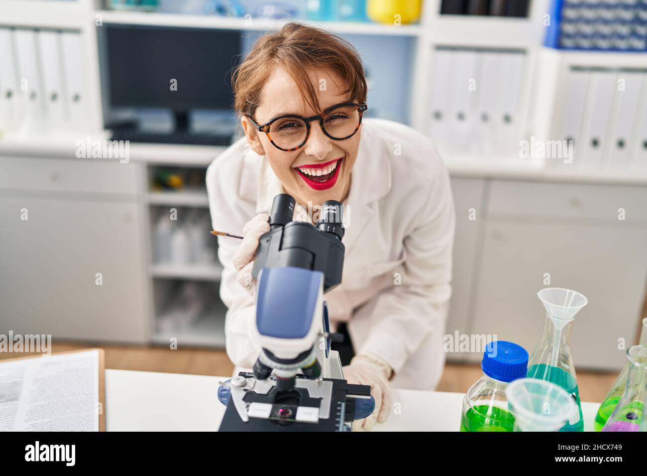 Young caucasian woman wearing scientist uniform using microscope at ...