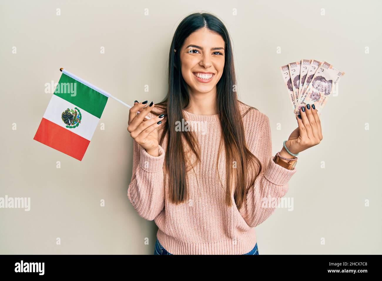 Young hispanic woman holding mexico flag and mexican pesos banknotes ...