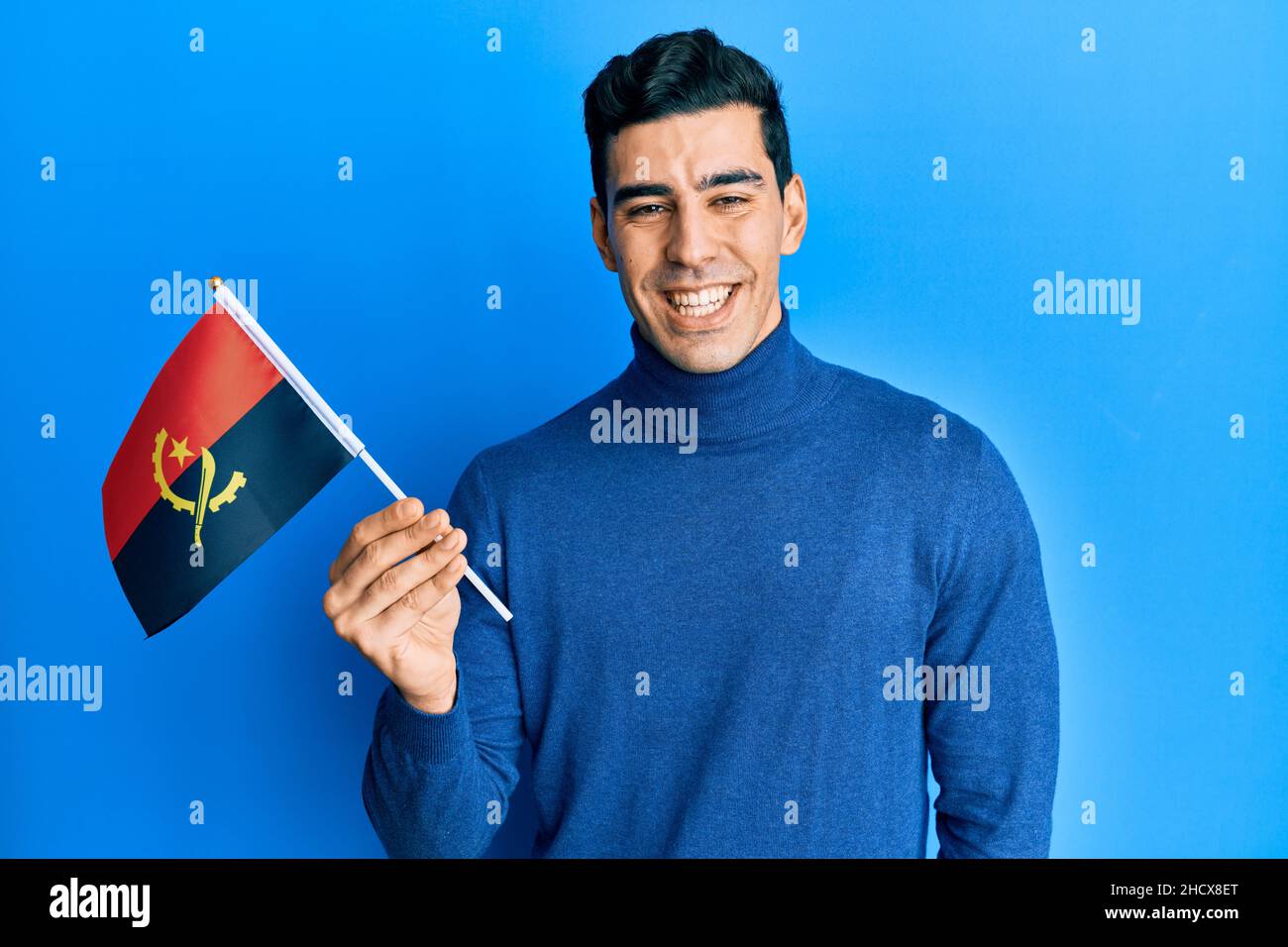 Handsome hispanic man holding angola flag looking positive and happy ...