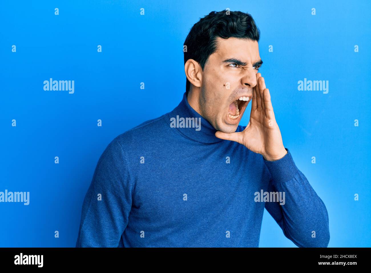 Handsome hispanic man wearing turtleneck sweater shouting and screaming ...