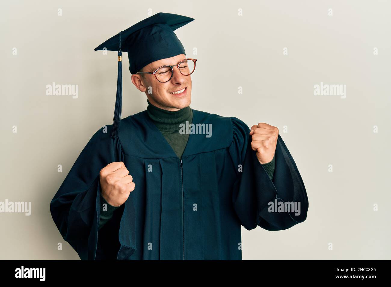 Young caucasian man wearing graduation cap and ceremony robe excited ...