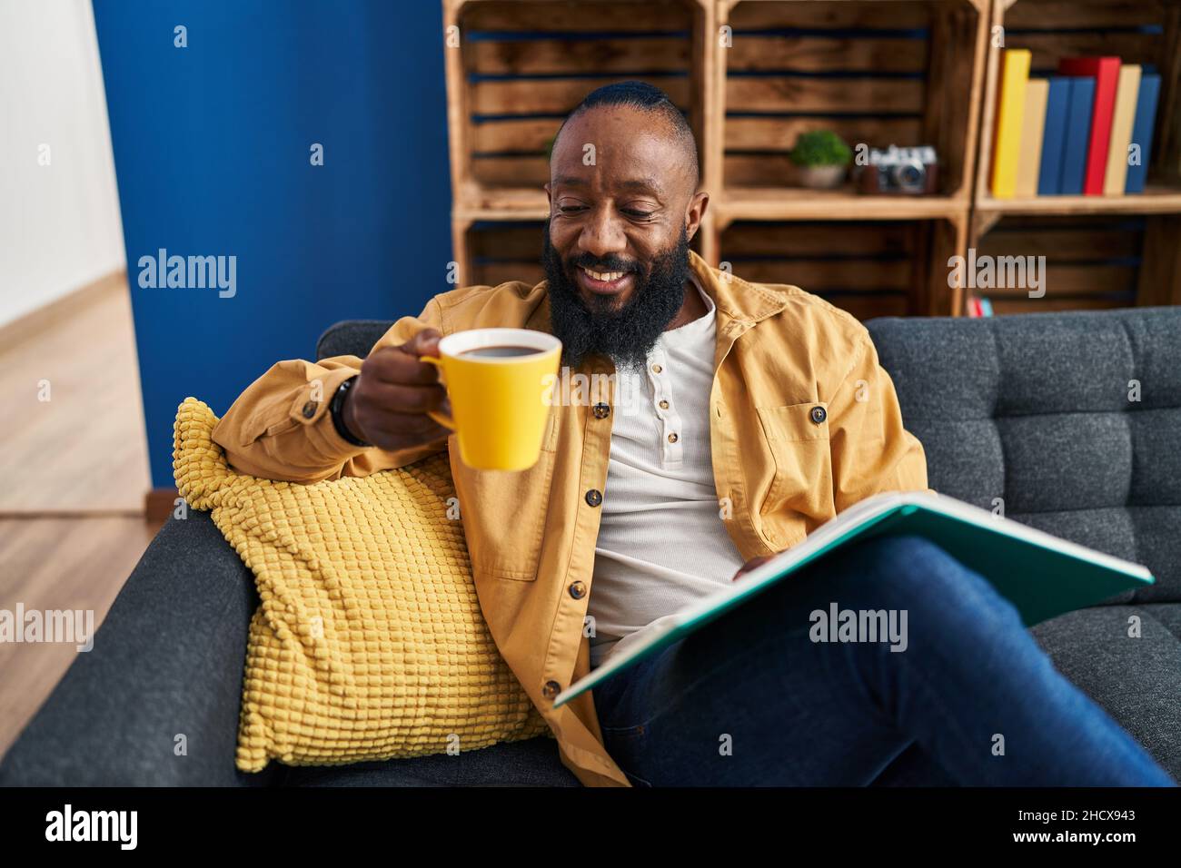 Young african american man reading book and drinking coffee at home ...