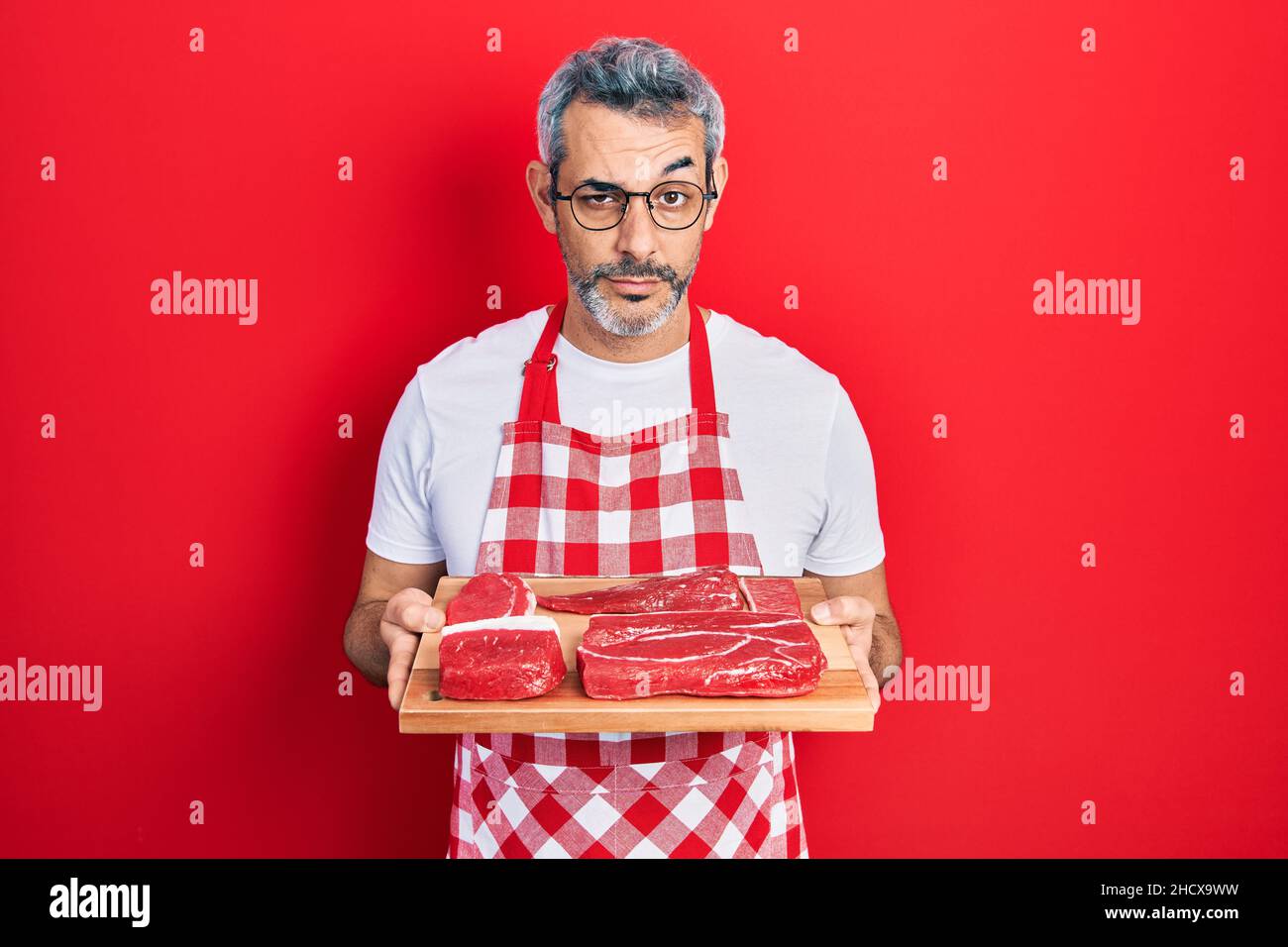 Handsome middle age man with grey hair wearing apron holding board with ...