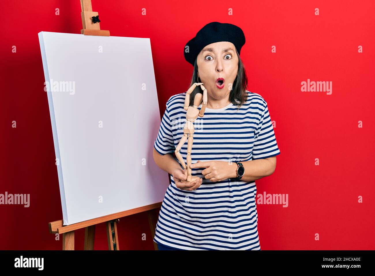 Middle age hispanic woman standing by painter easel stand holding ...