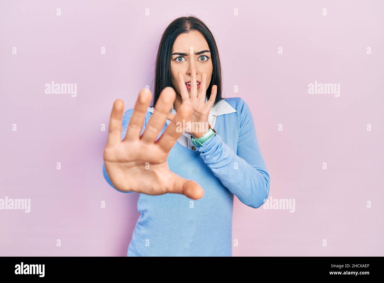 Beautiful woman with blue eyes standing over pink background afraid and ...
