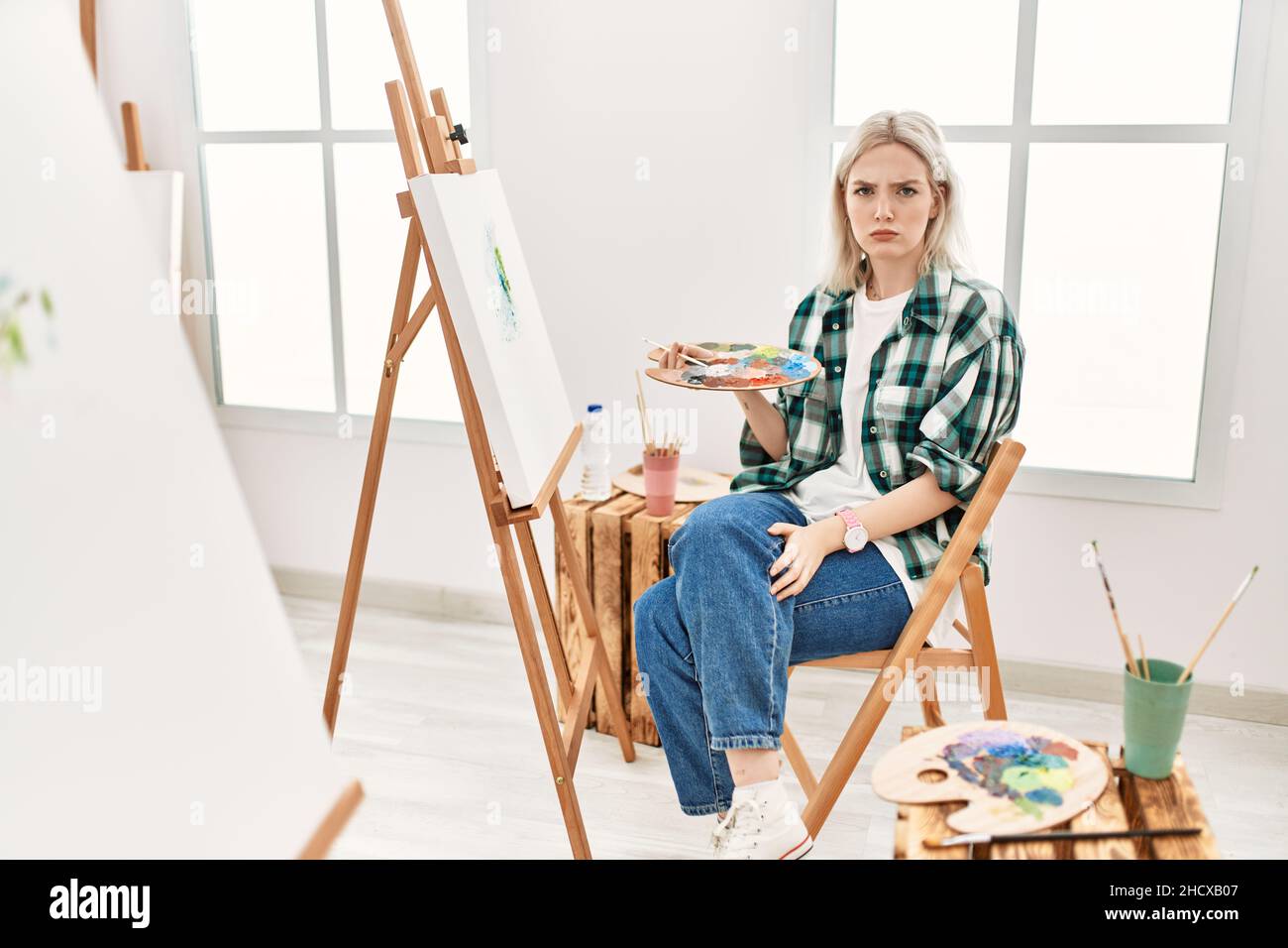 Young artist woman painting on canvas at art studio skeptic and nervous ...