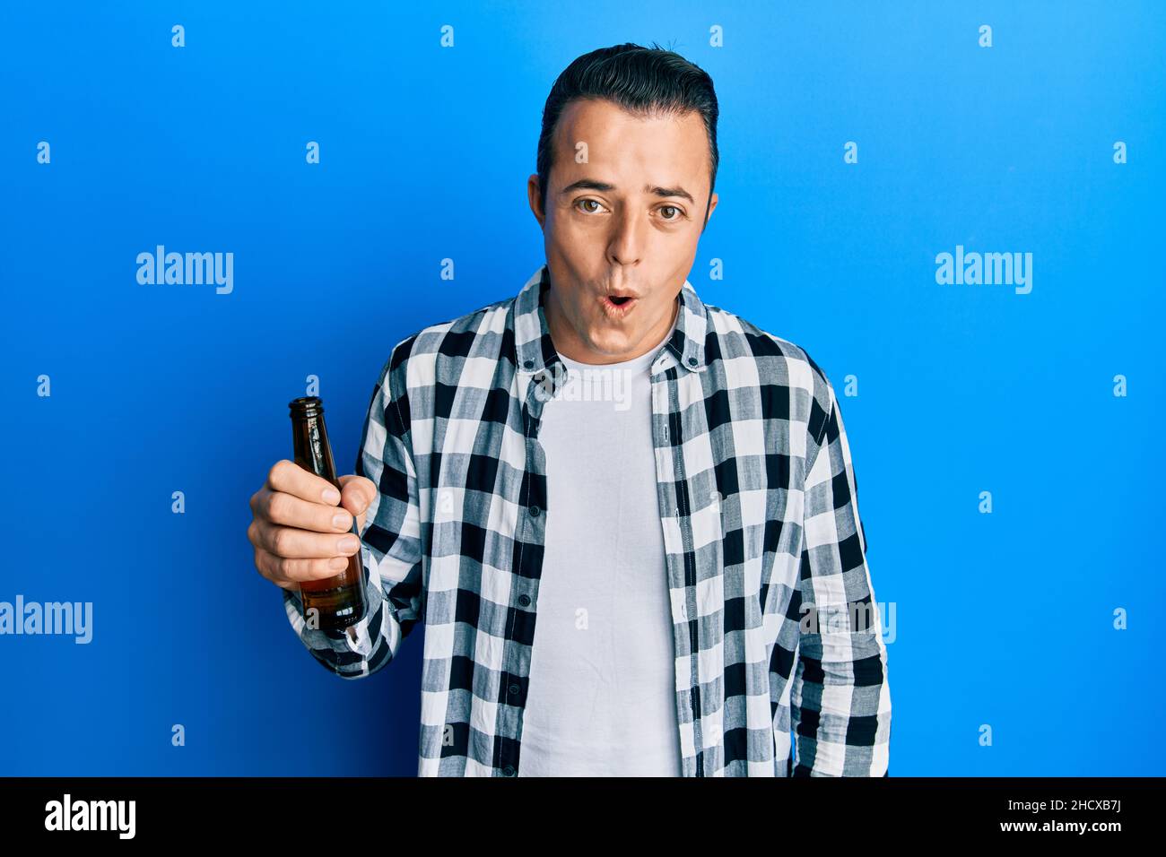 Handsome young man drinking a pint of beer scared and amazed with open ...