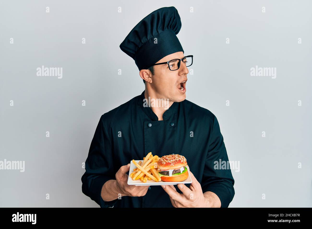 Handsome young man chef holding burger with fries angry and mad ...
