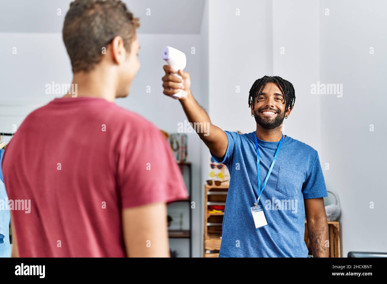 Two men shopkeeper and customer measuring temperature at clothing store ...