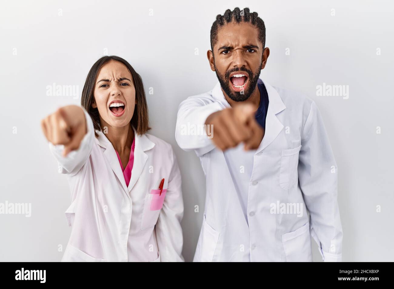 Young hispanic doctors standing over white background pointing ...