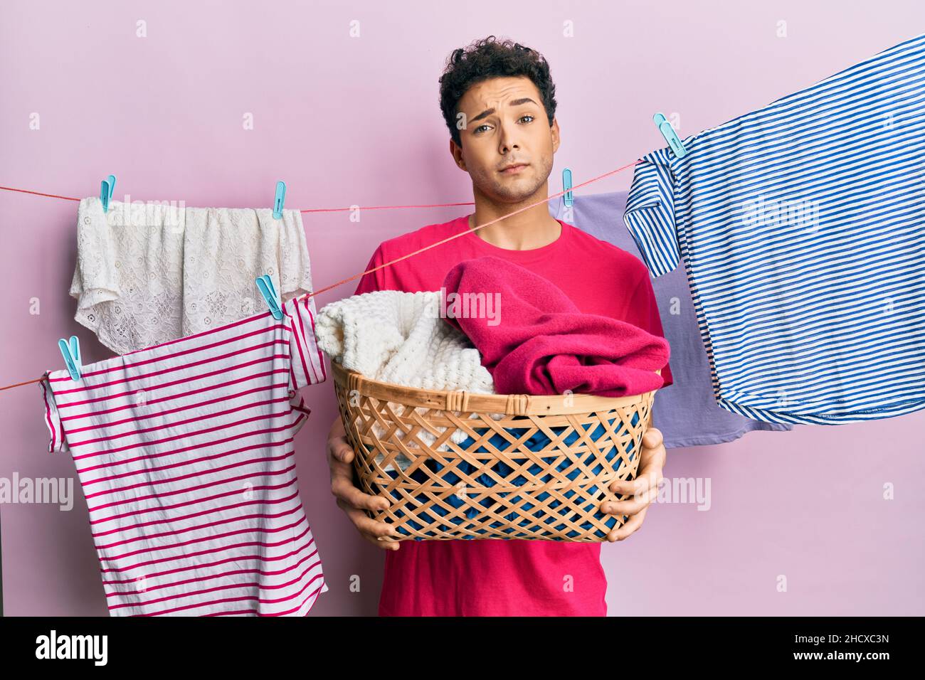 Handsome hispanic man doing laundry holding wicker basket in shock face ...