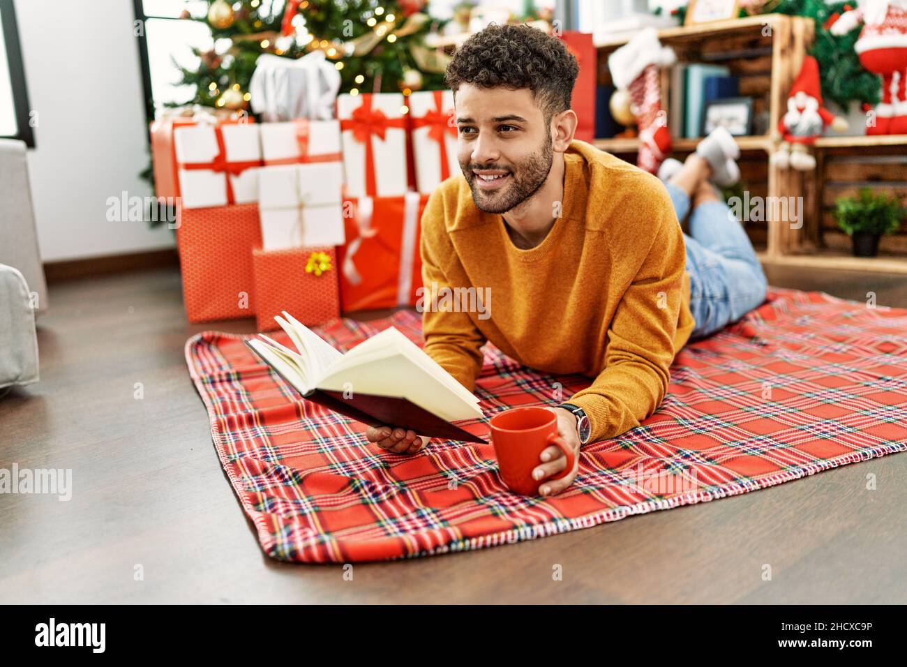 Young arab man reading book and drinking coffee lying on the floor by ...