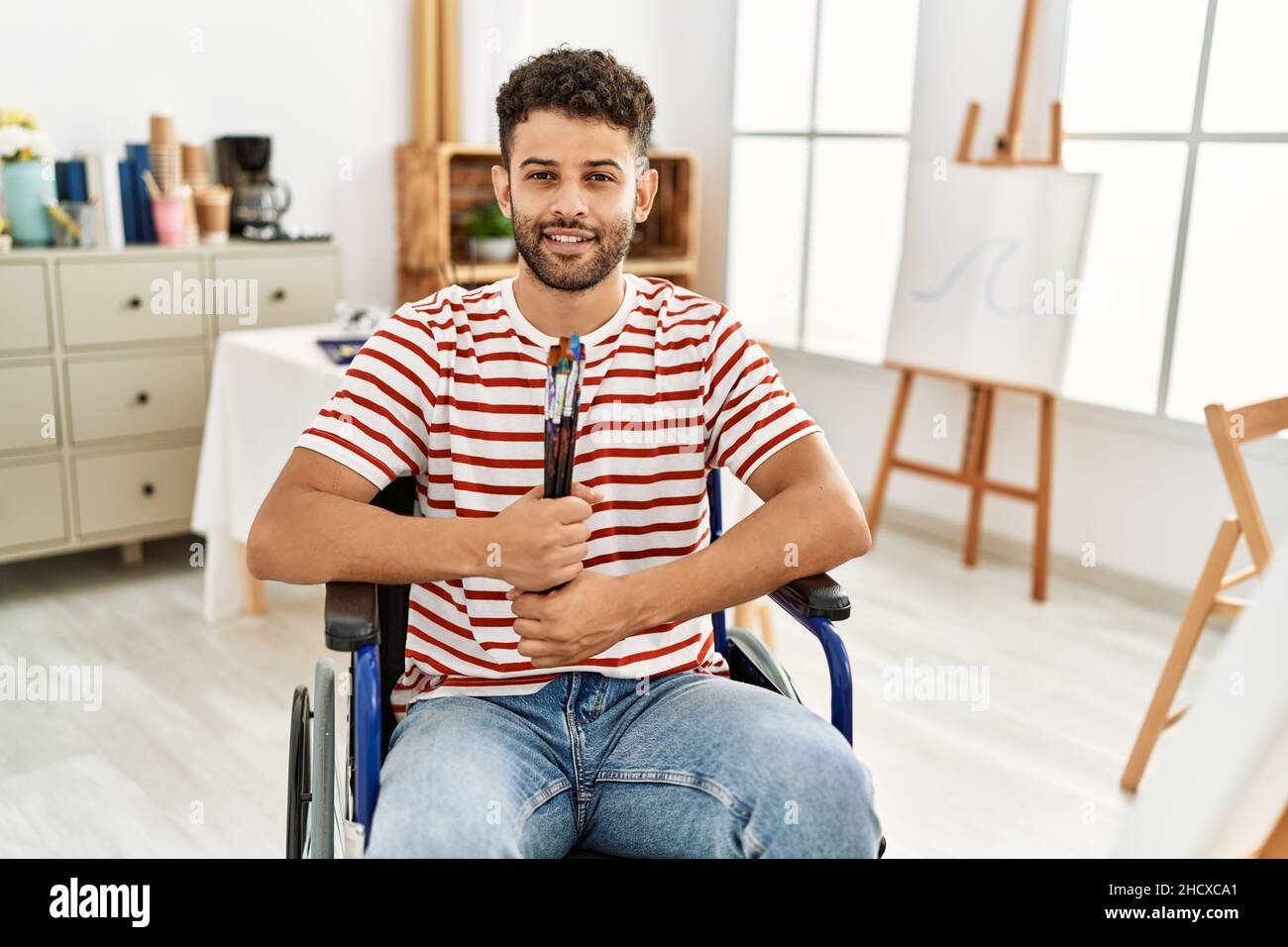 Young arab disabled artist man holding paintbrushes sitting on ...