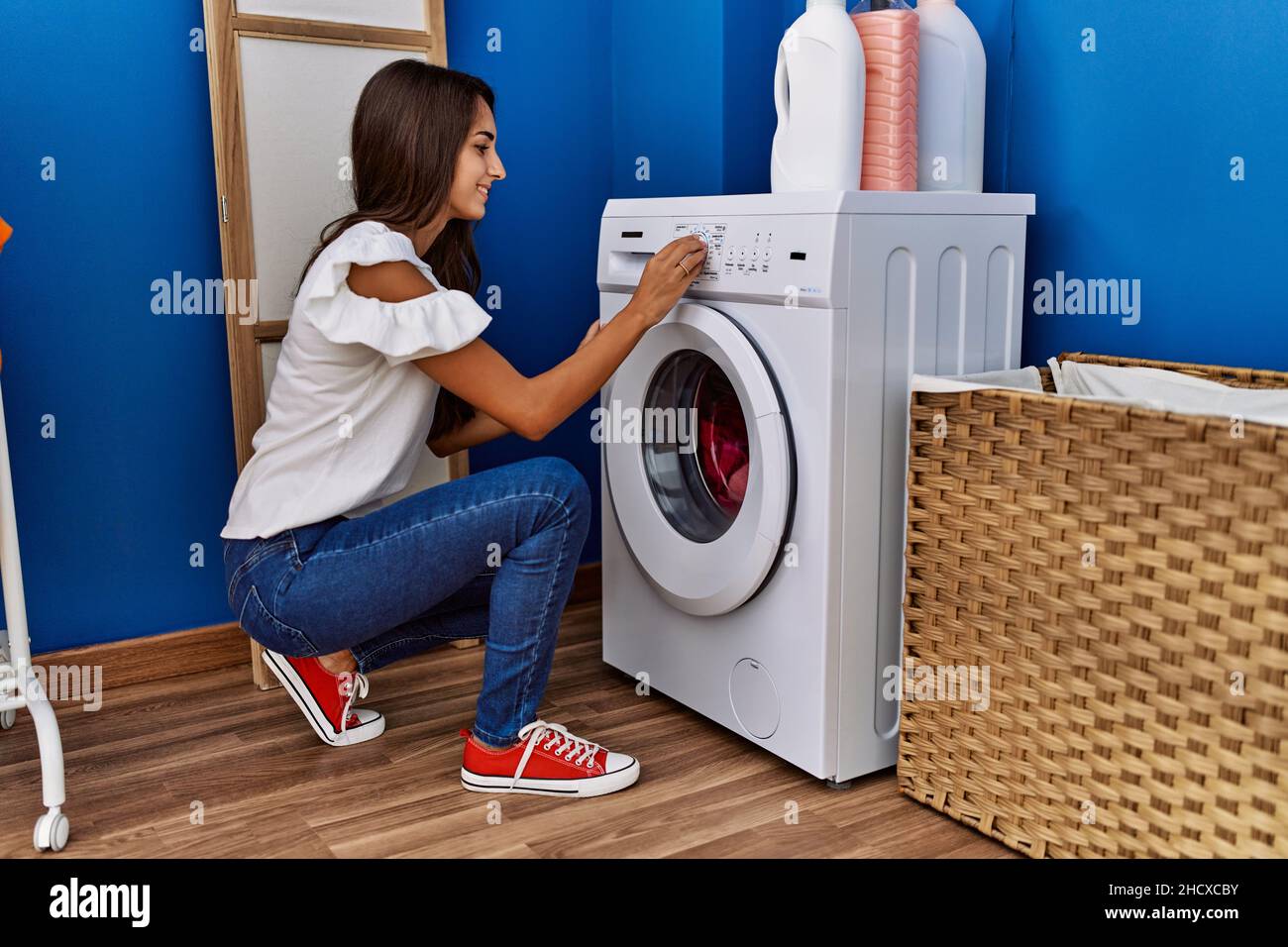 Young hispanic woman cleaning clothes using washing machine at laundry ...