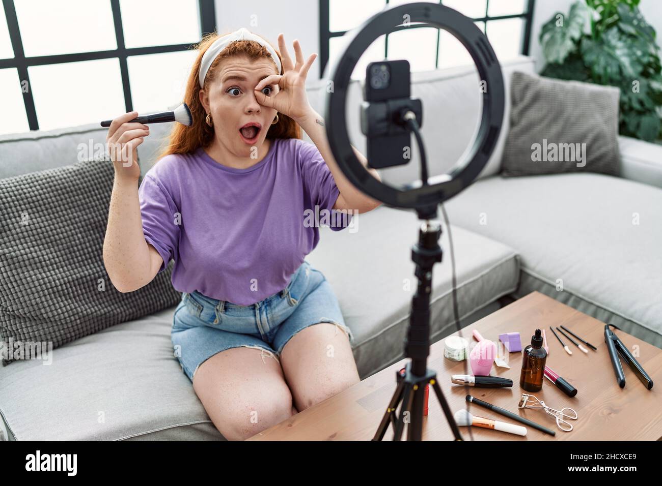 Young redhead woman recording make up tutorial with smartphone at home ...