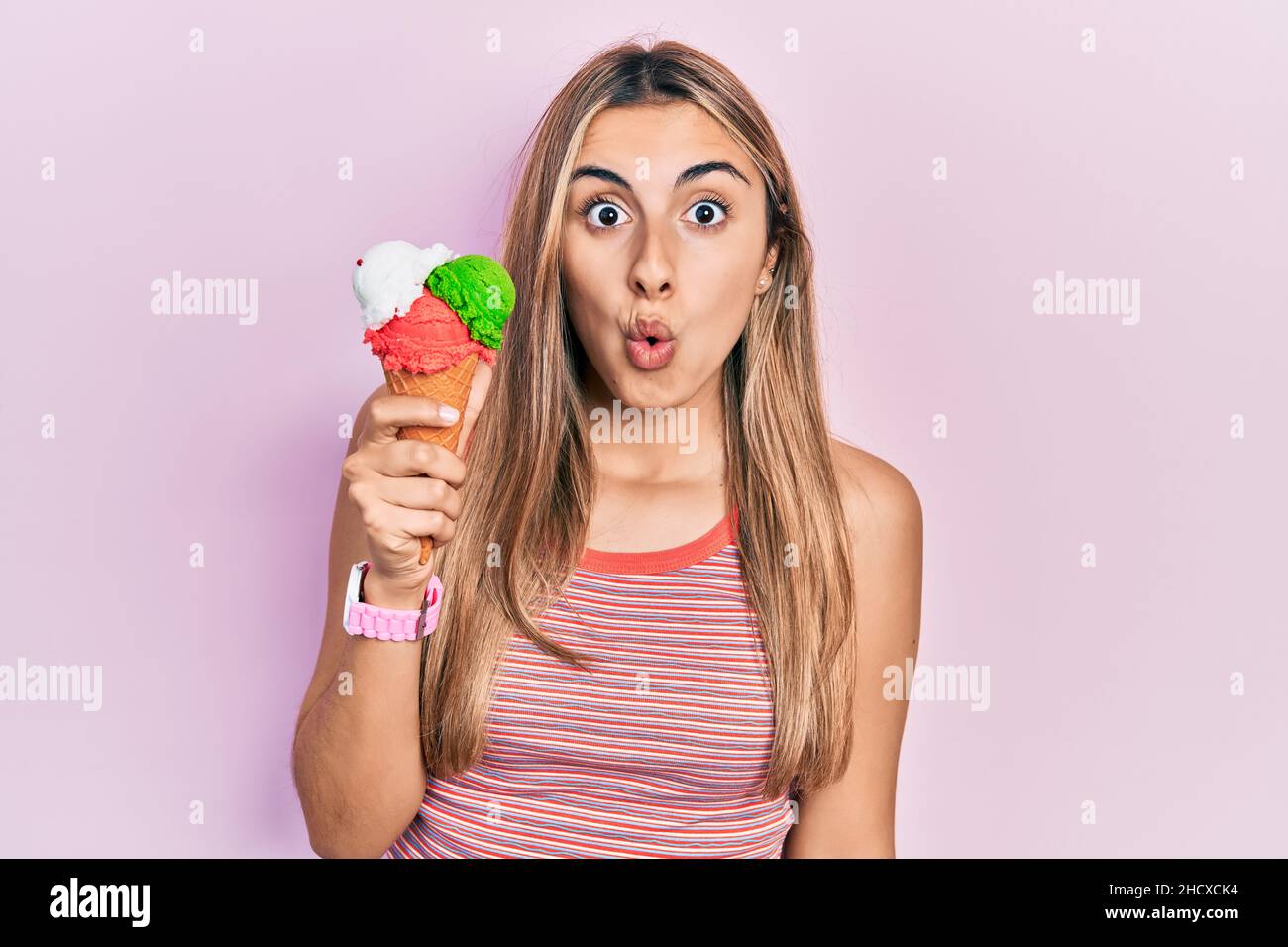 Beautiful hispanic woman holding ice cream scared and amazed with open ...