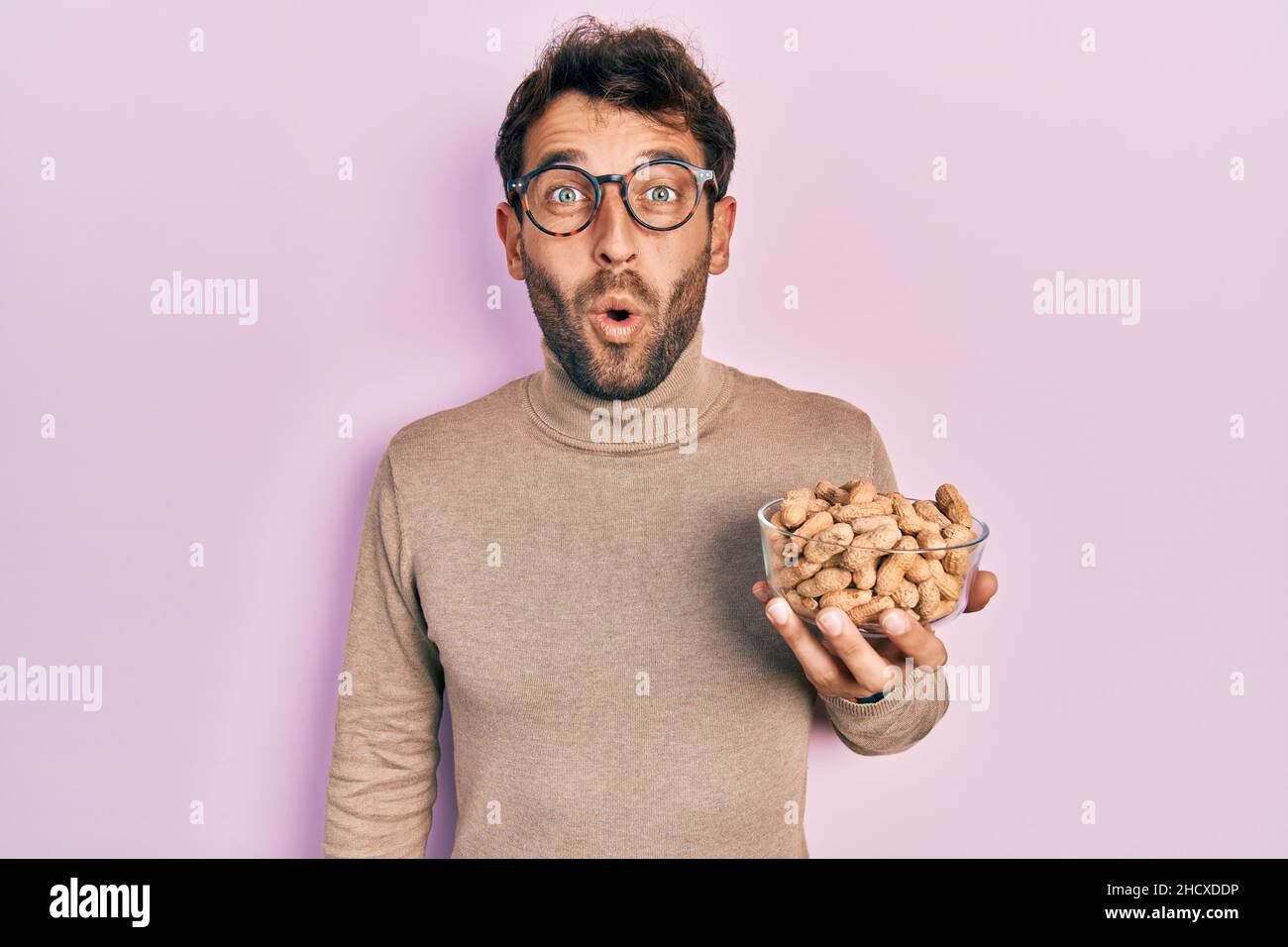 Handsome man with beard holding peanuts scared and amazed with open ...
