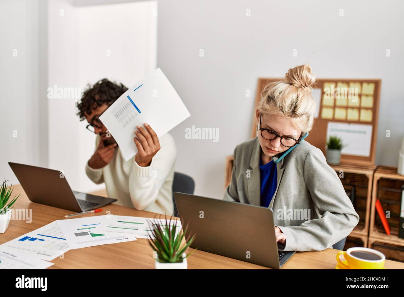 Two business workers talking on the smartphone and using laptop at the ...