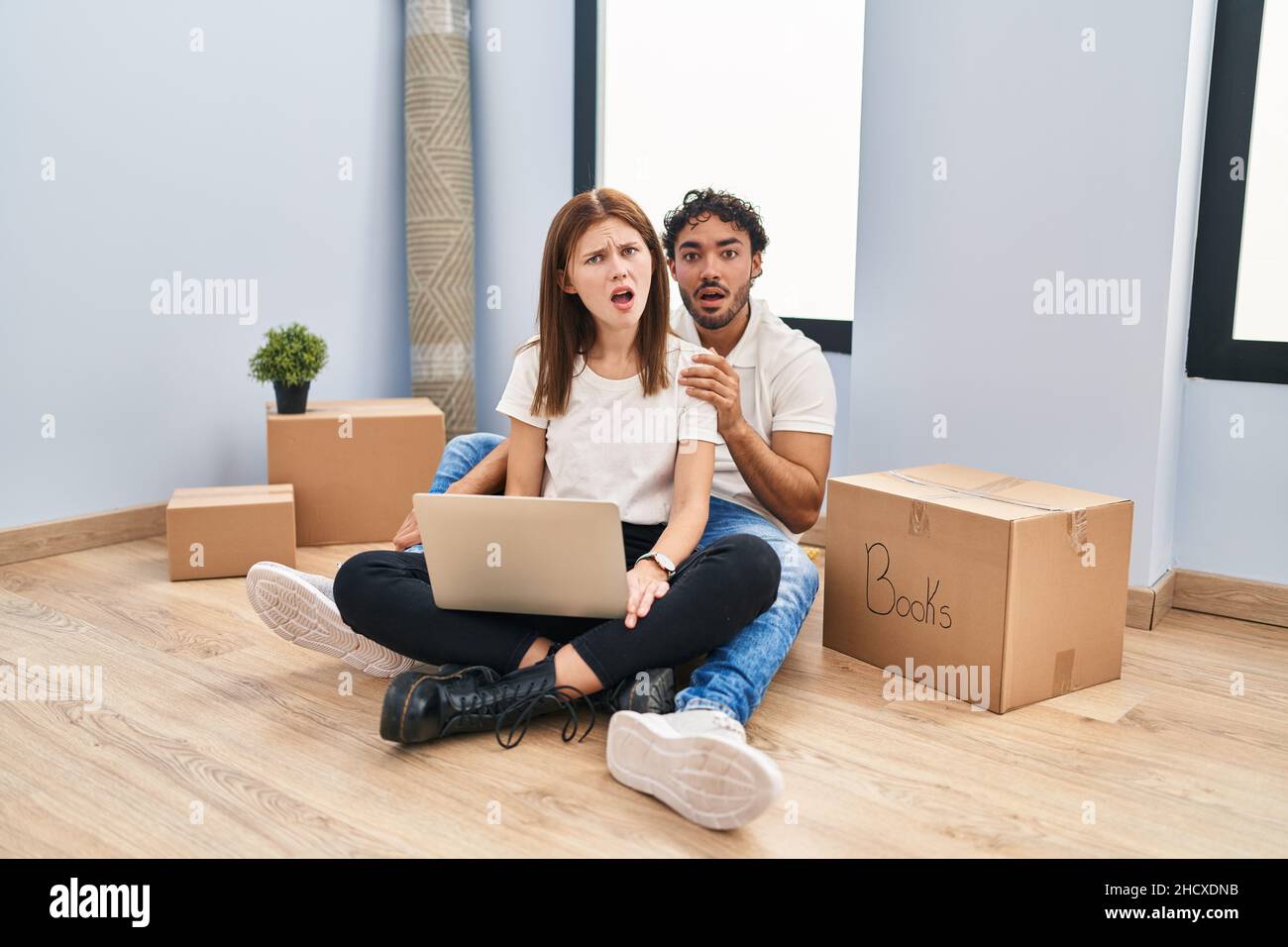 Young couple using laptop at new home in shock face, looking skeptical ...