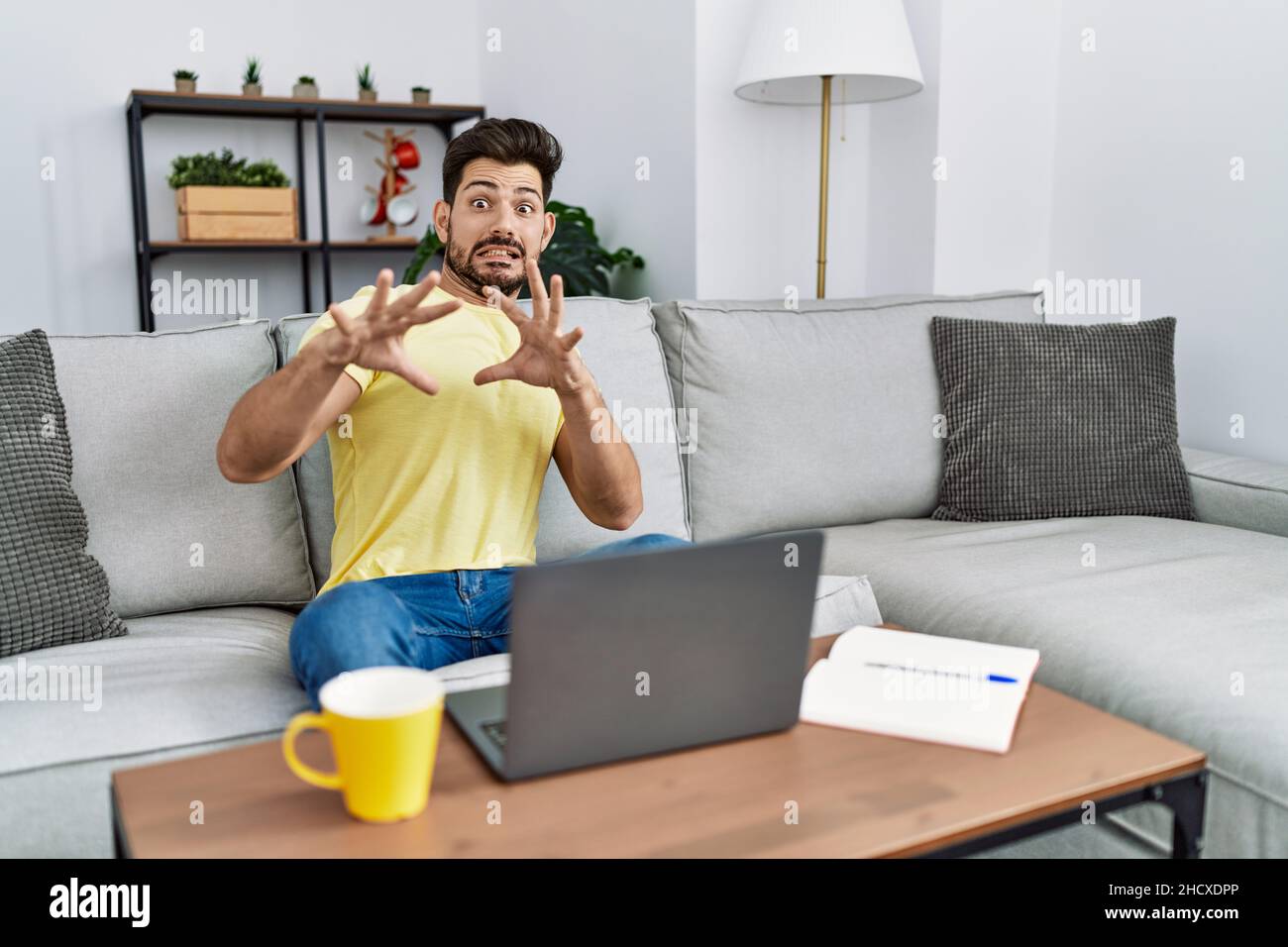 Young man with beard using laptop at home afraid and terrified with ...