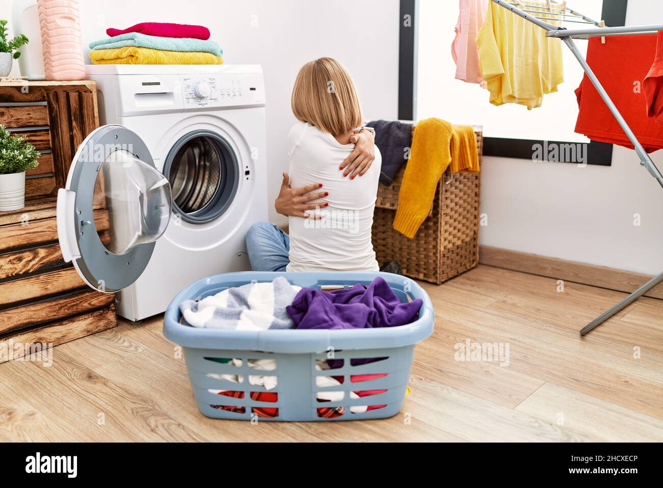Young caucasian woman doing laundry with clothes in the basket hugging ...
