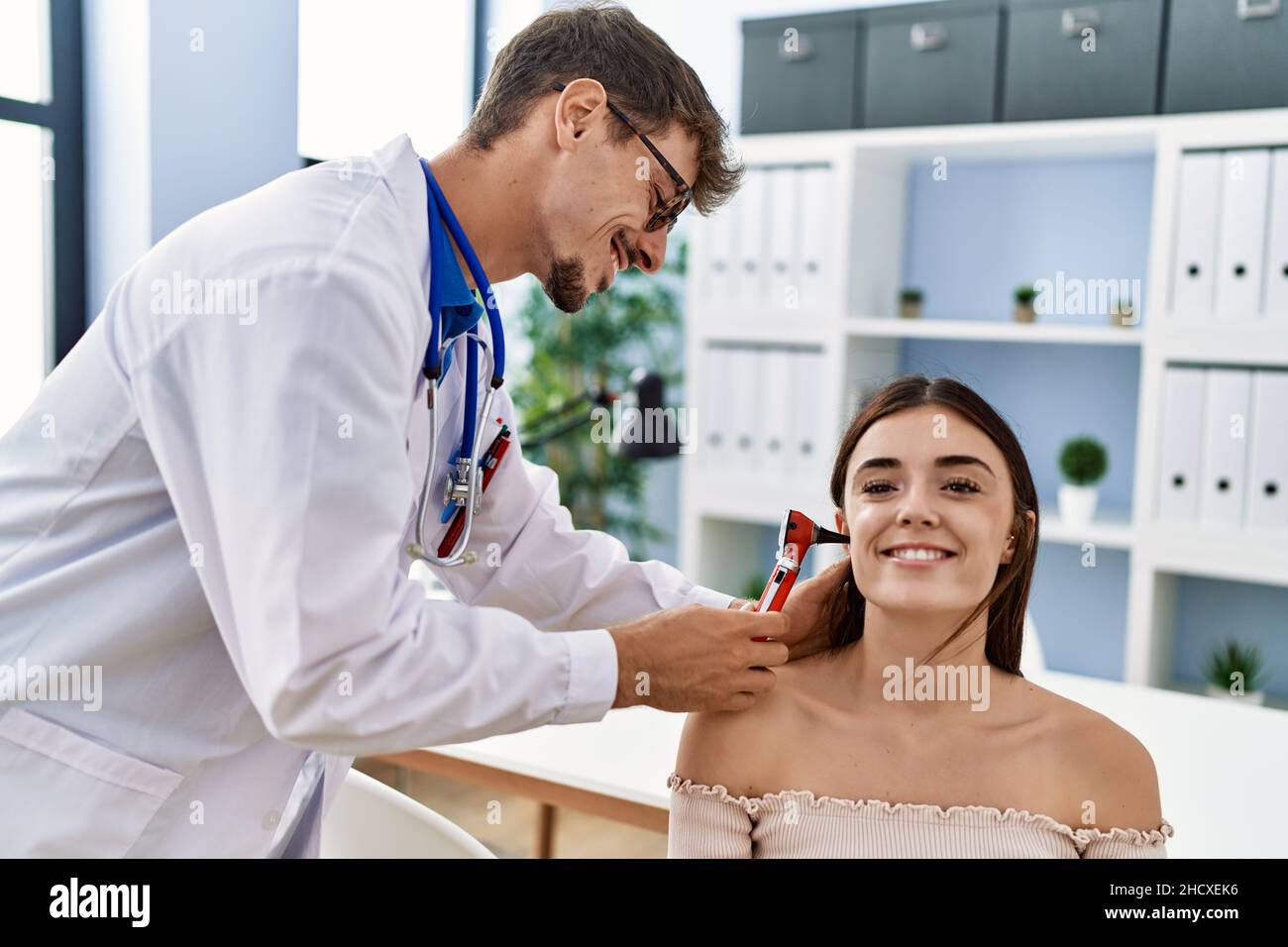 Man and woman wearing doctor uniform auscultating ear using otoscope at ...