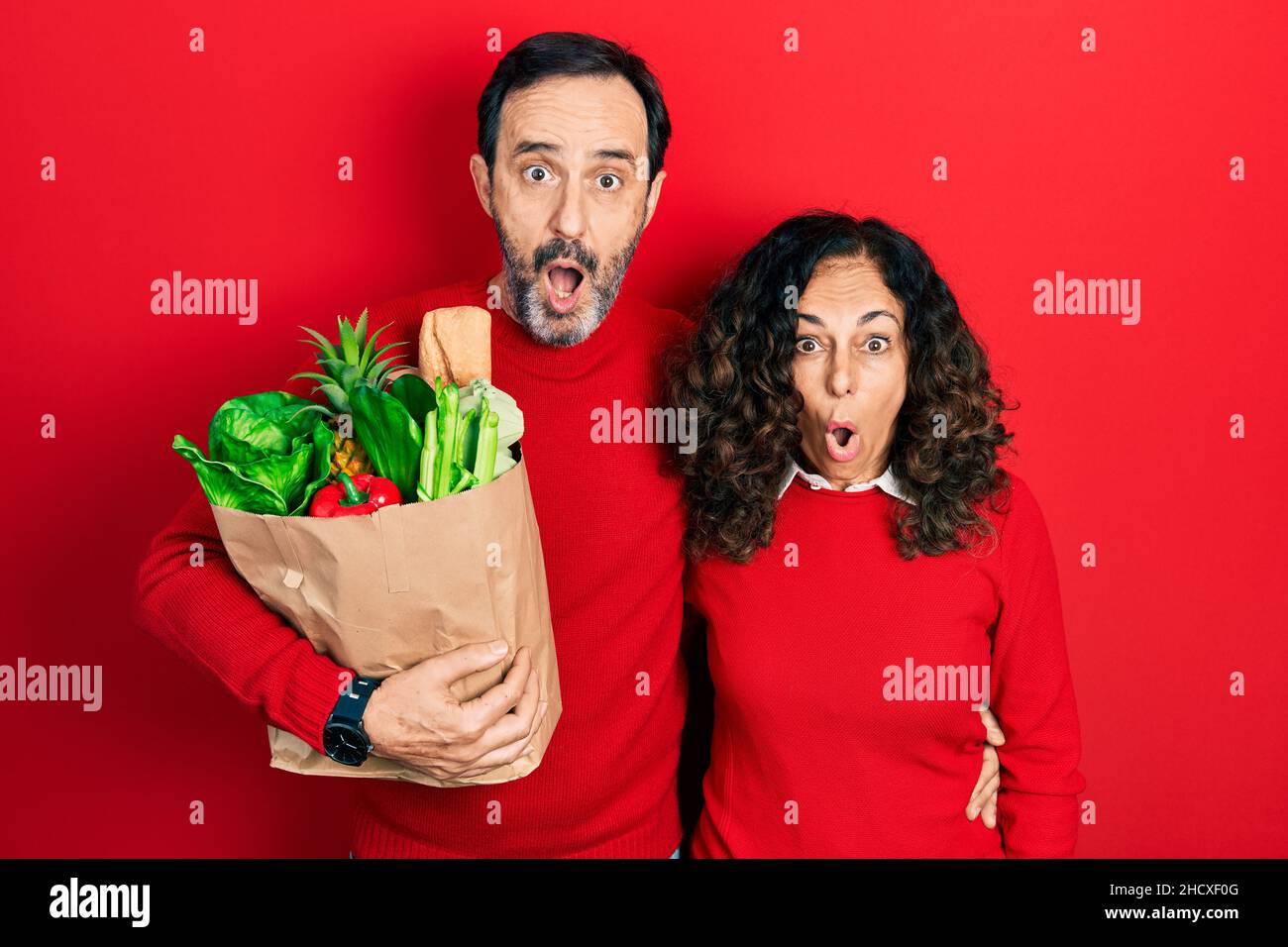 Middle age couple of hispanic woman and man holding paper bag with ...