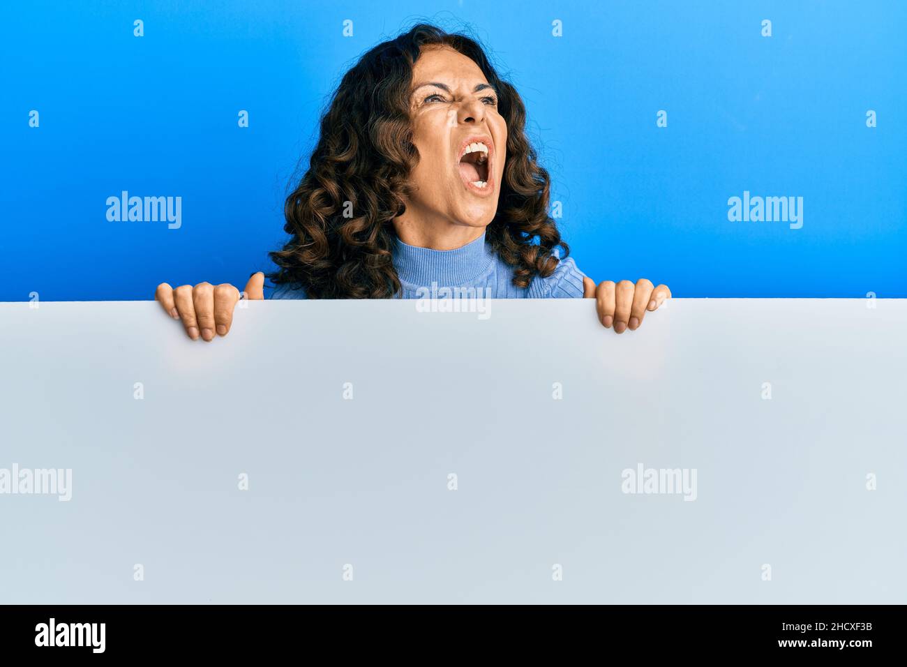 Middle age hispanic woman holding blank empty banner angry and mad ...