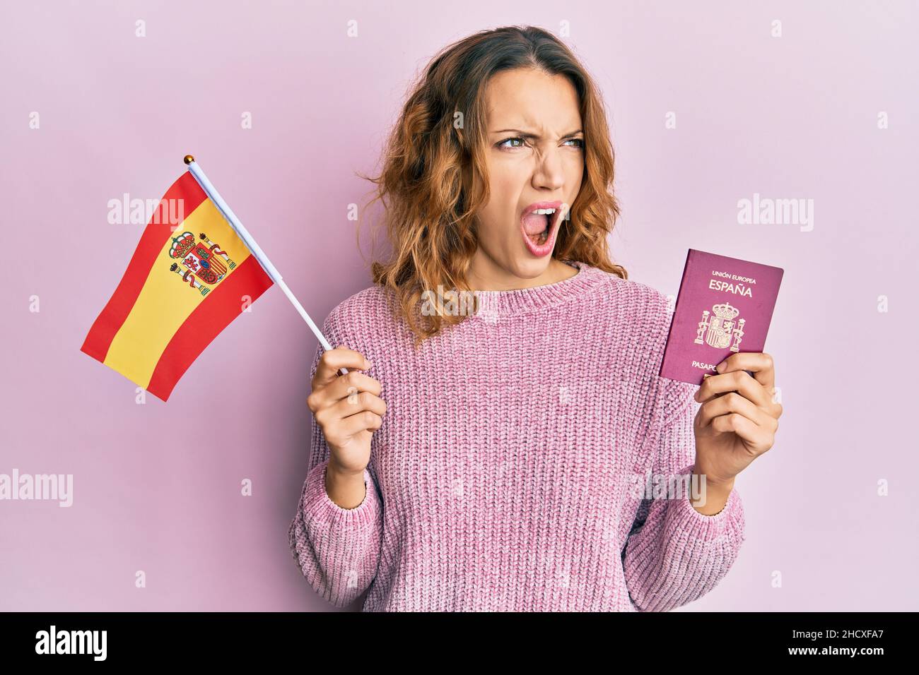 Young caucasian woman holding spain flag and passport angry and mad ...
