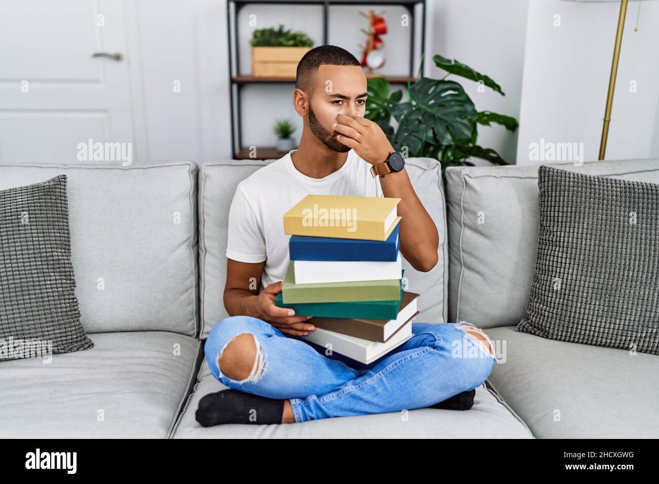 African american young man holding a pile of books sitting on the sofa ...