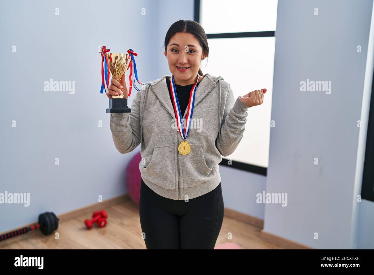 Young latin woman holding winner trophy screaming proud, celebrating ...