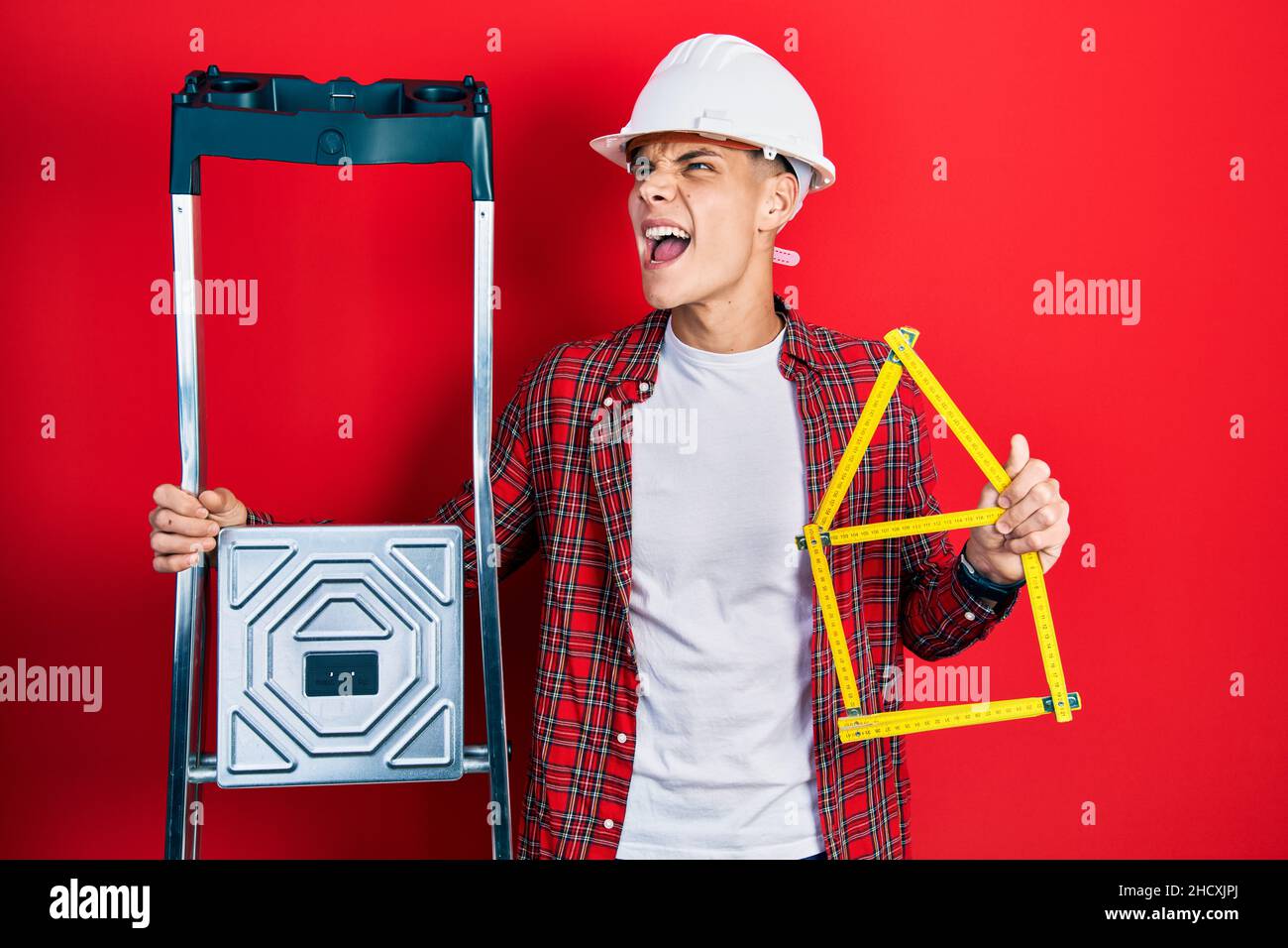 Young hispanic man wearing handyman uniform holding construction stairs ...