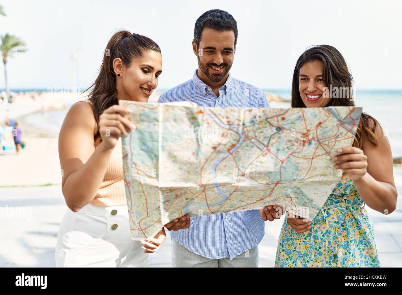 Three young hispanic friends smiling happy searching route on city map ...