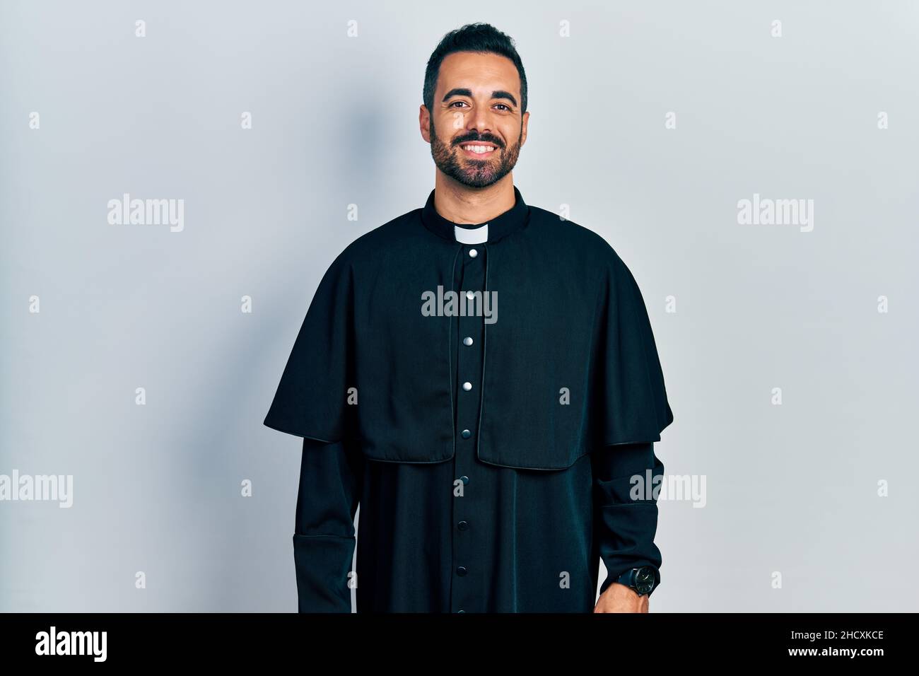 Handsome hispanic man with beard wearing catholic priest robe with a ...