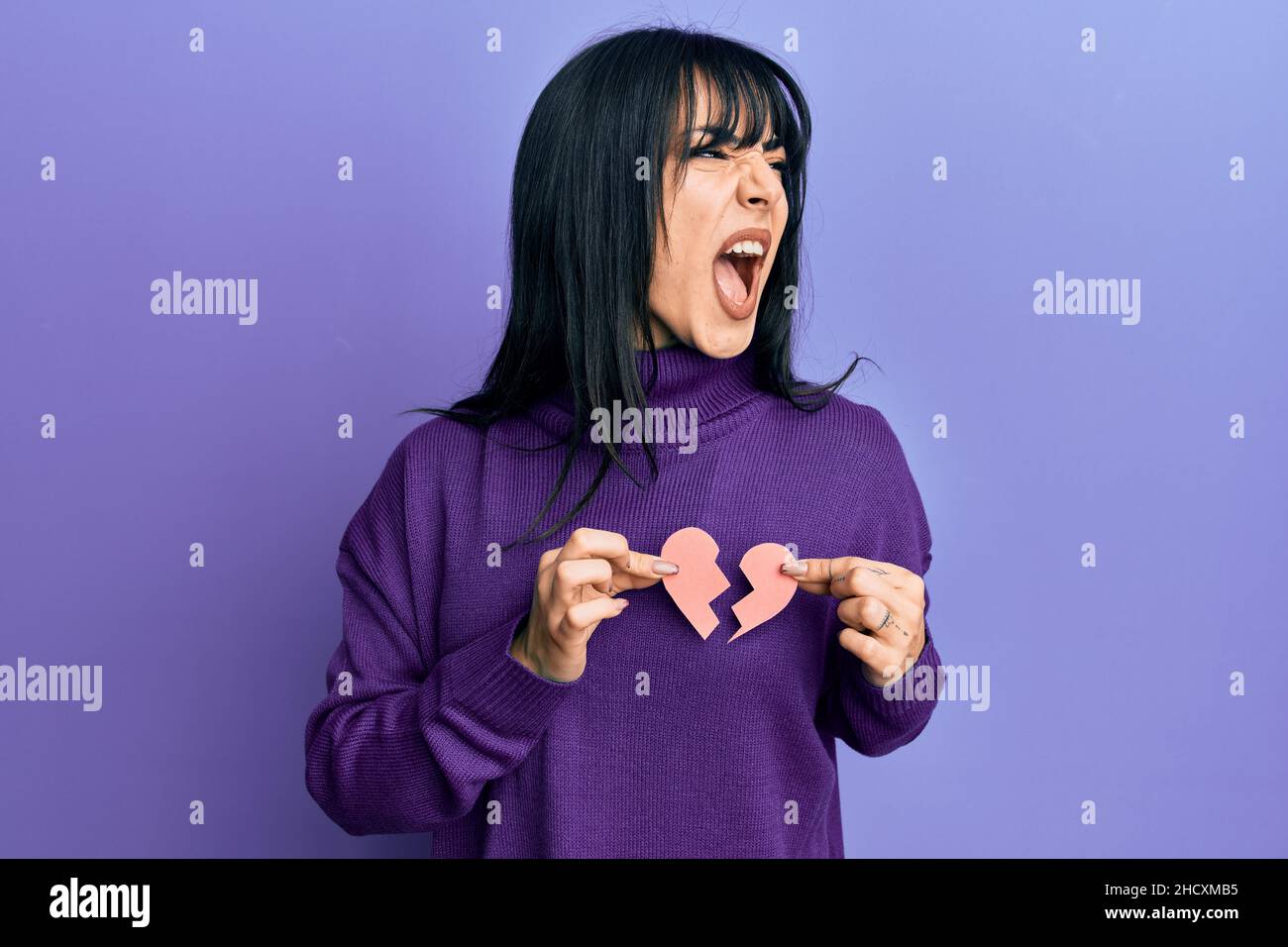 Young brunette woman with bangs holding broken heart paper shape angry ...