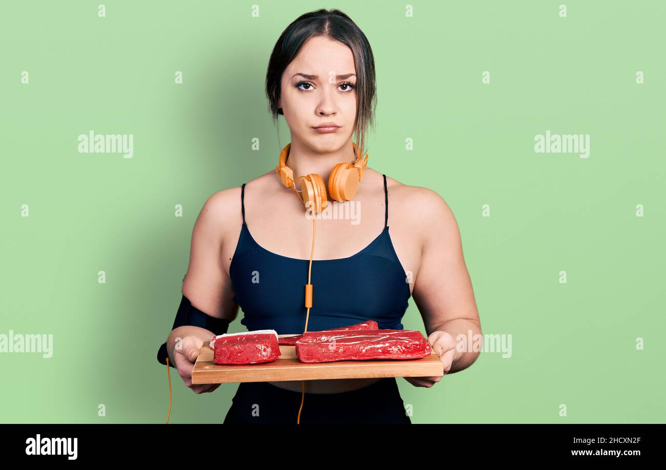 Young hispanic girl wearing workout clothes and holding meat board ...