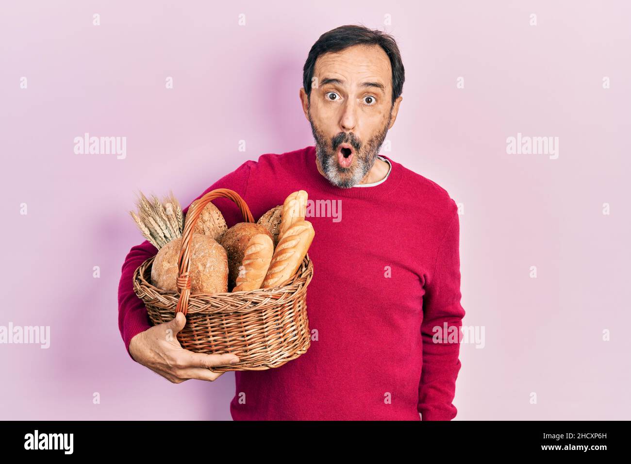Middle age hispanic man holding wicker basket with bread scared and ...