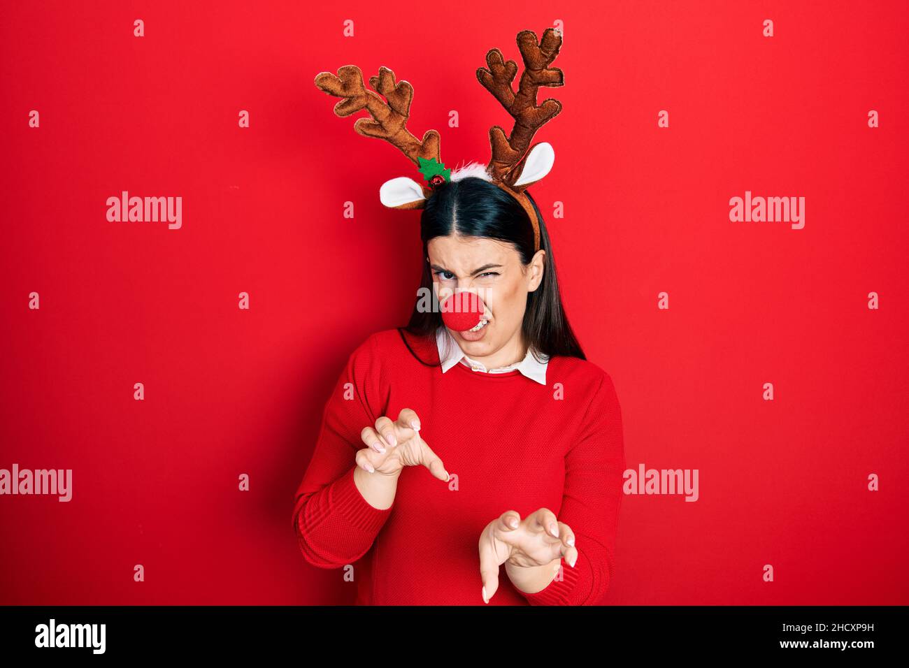 Young hispanic woman wearing deer christmas hat and red nose disgusted ...