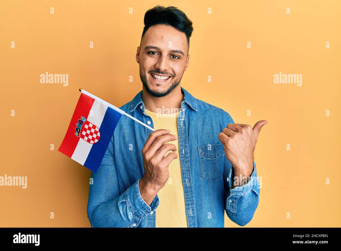 Young arab man holding croatia flag pointing thumb up to the side ...