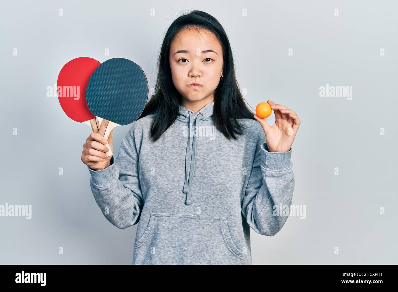 Young chinese girl holding red ping pong rackets and ball puffing ...