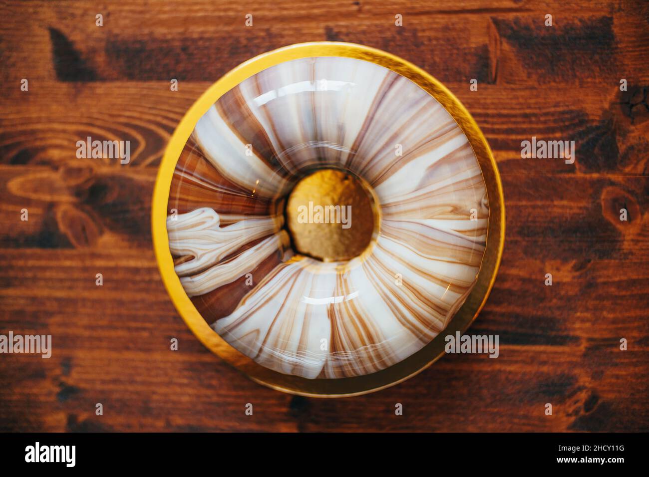 Round mousse cake with marble icing on a gold plate on the table. Top ...