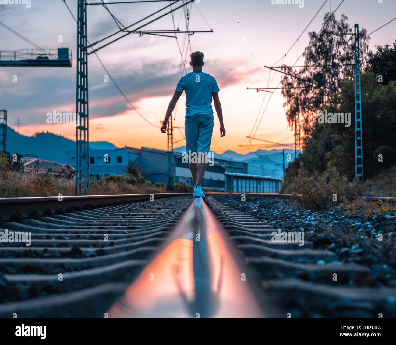 Back view of a young Caucasian man walking on the railroad at sunset in ...