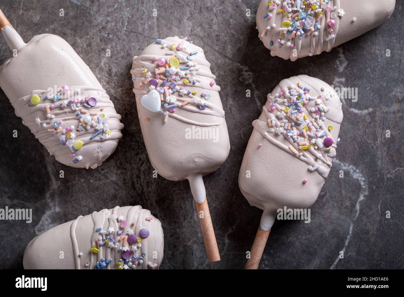 Cold and sweet popsicles with white chocolate topping on dark stone ...