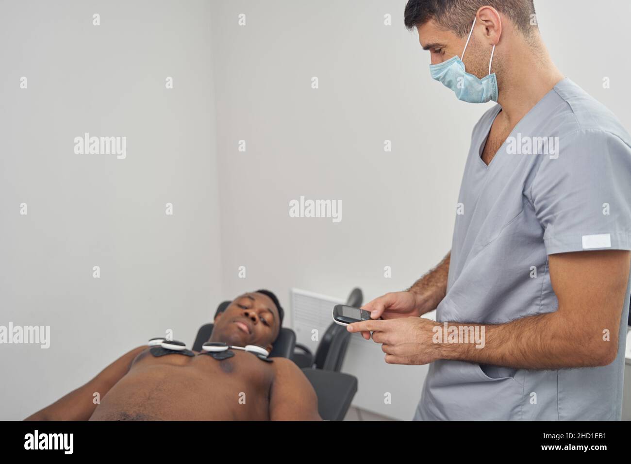 Physiotherapist applying electrical muscular stimulation device on man ...