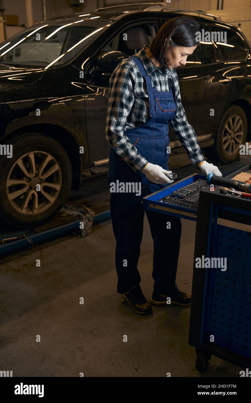Concentrated repair shop worker searching her toolbox for instruments ...