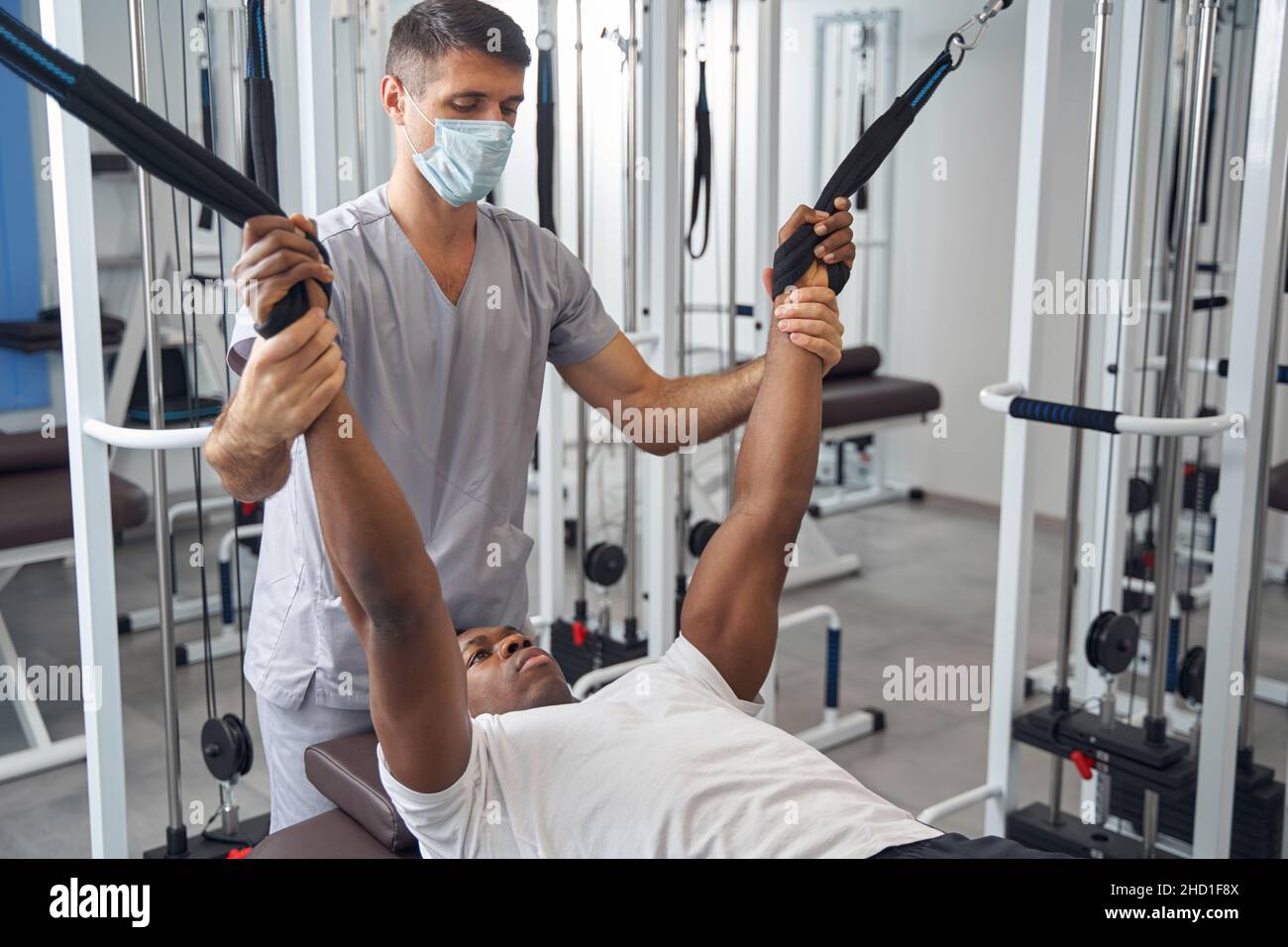 Male patient working out on gym equipment supervised by physiotherapist ...