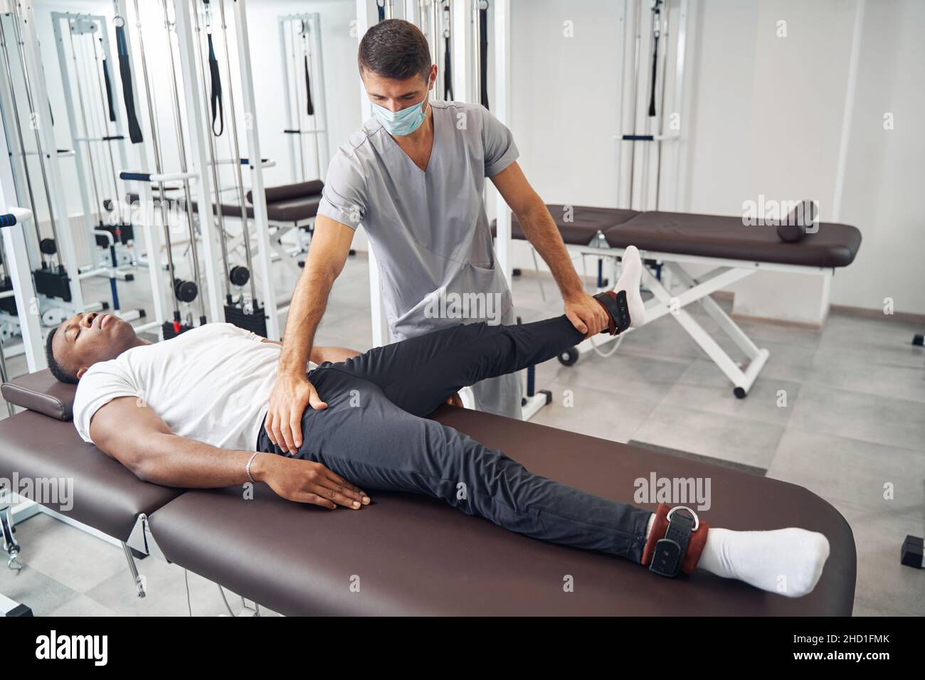 Concentrated certified physiotherapist performing hip abduction stretch ...