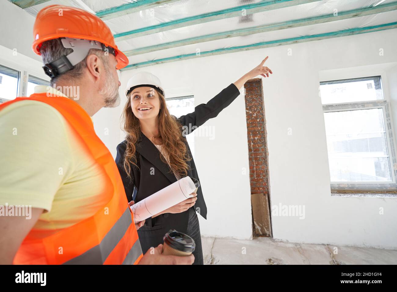 Female designing engineer turning to aged construction worker with ...